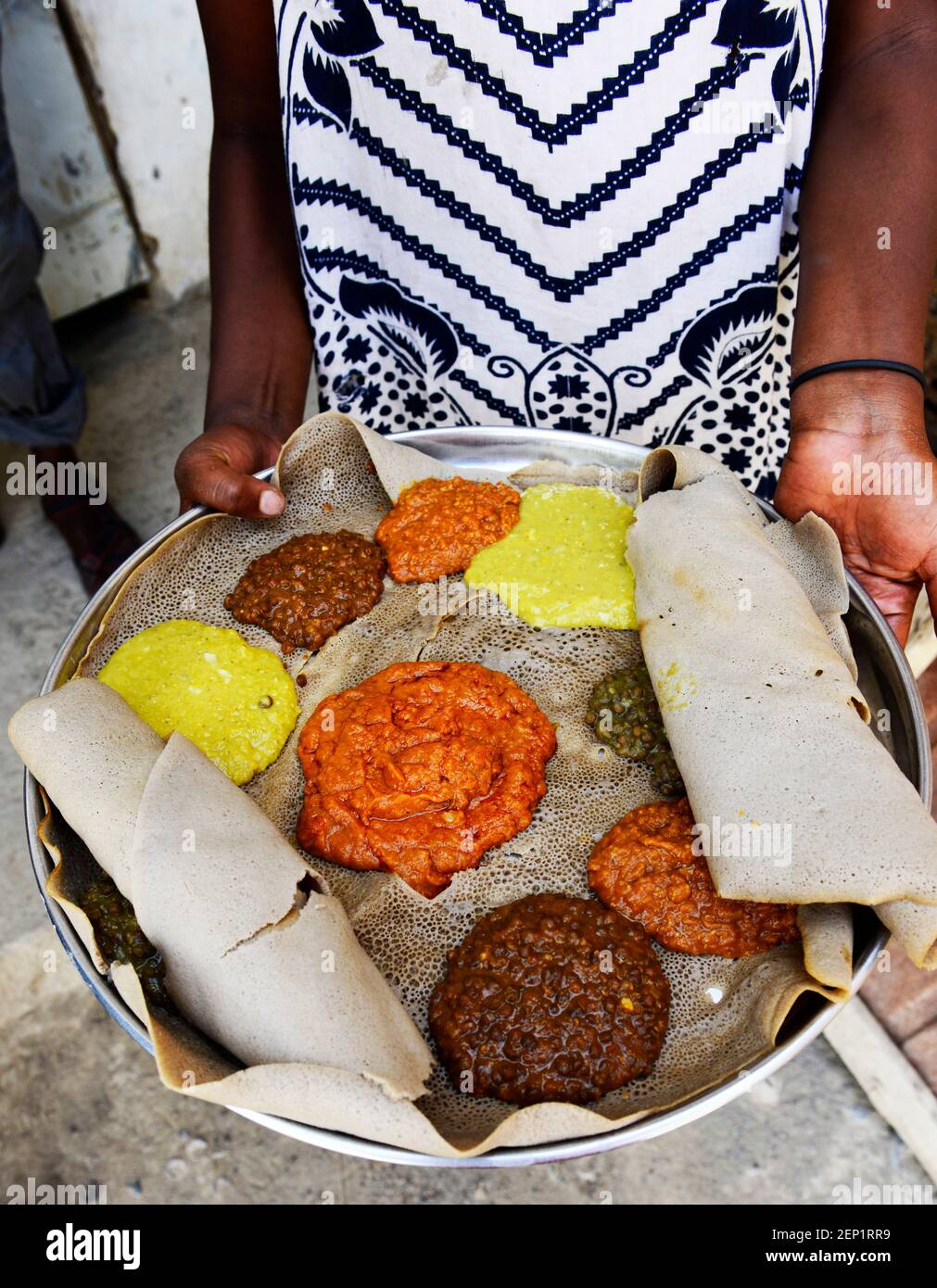 An Ethiopian waitress presenting a traditional Injera dish with variety ...