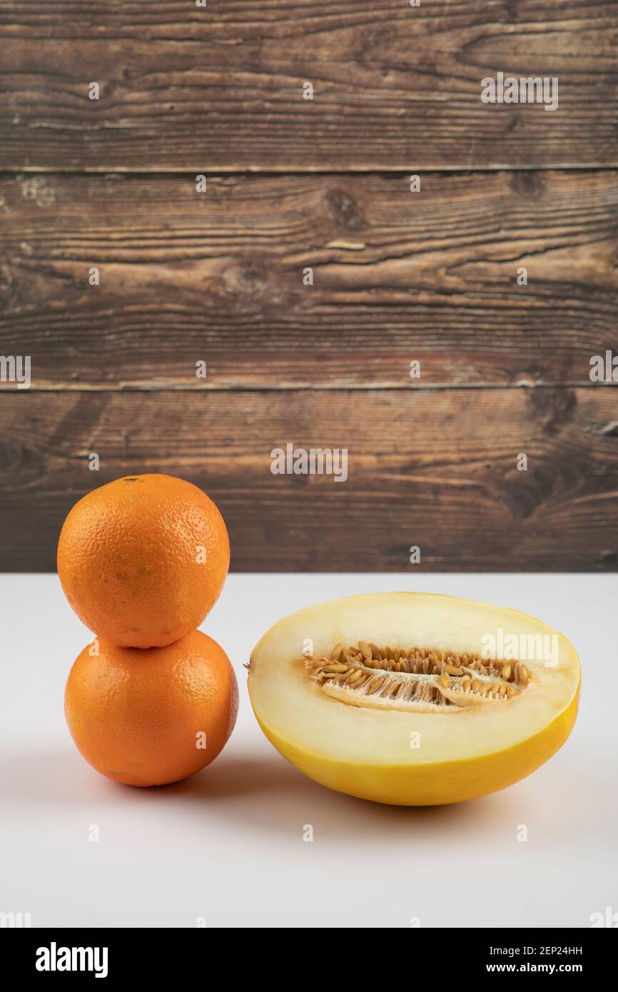 Two whole fresh oranges and sliced yellow melon on white table Stock ...
