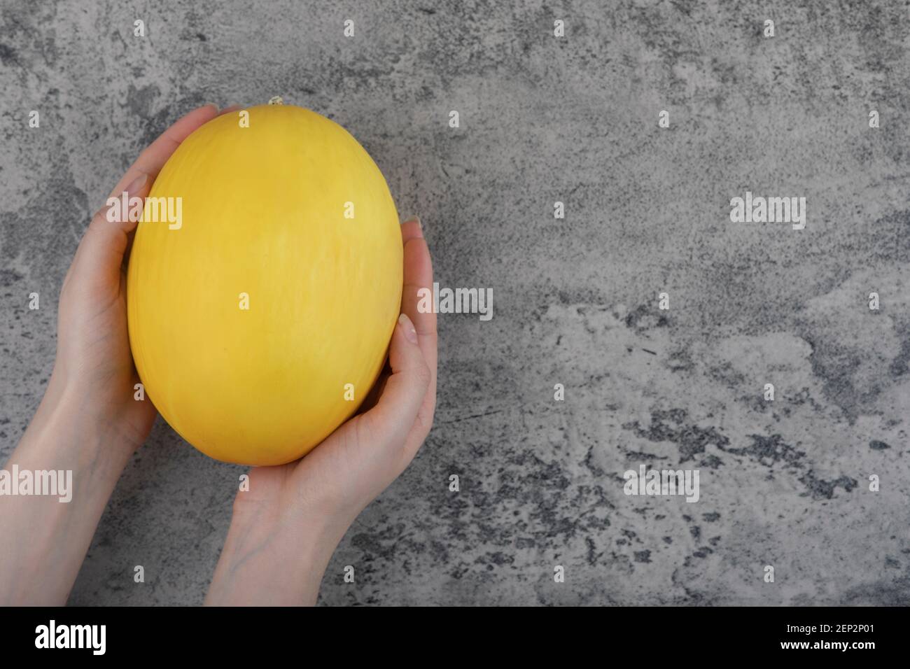 Female hand holding yellow melon on stone background Stock Photo - Alamy