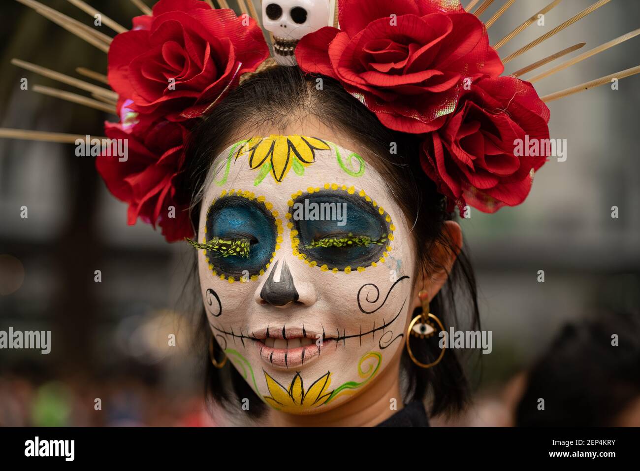 A woman with a brightly colored Catrina face paint poses for the camera ...