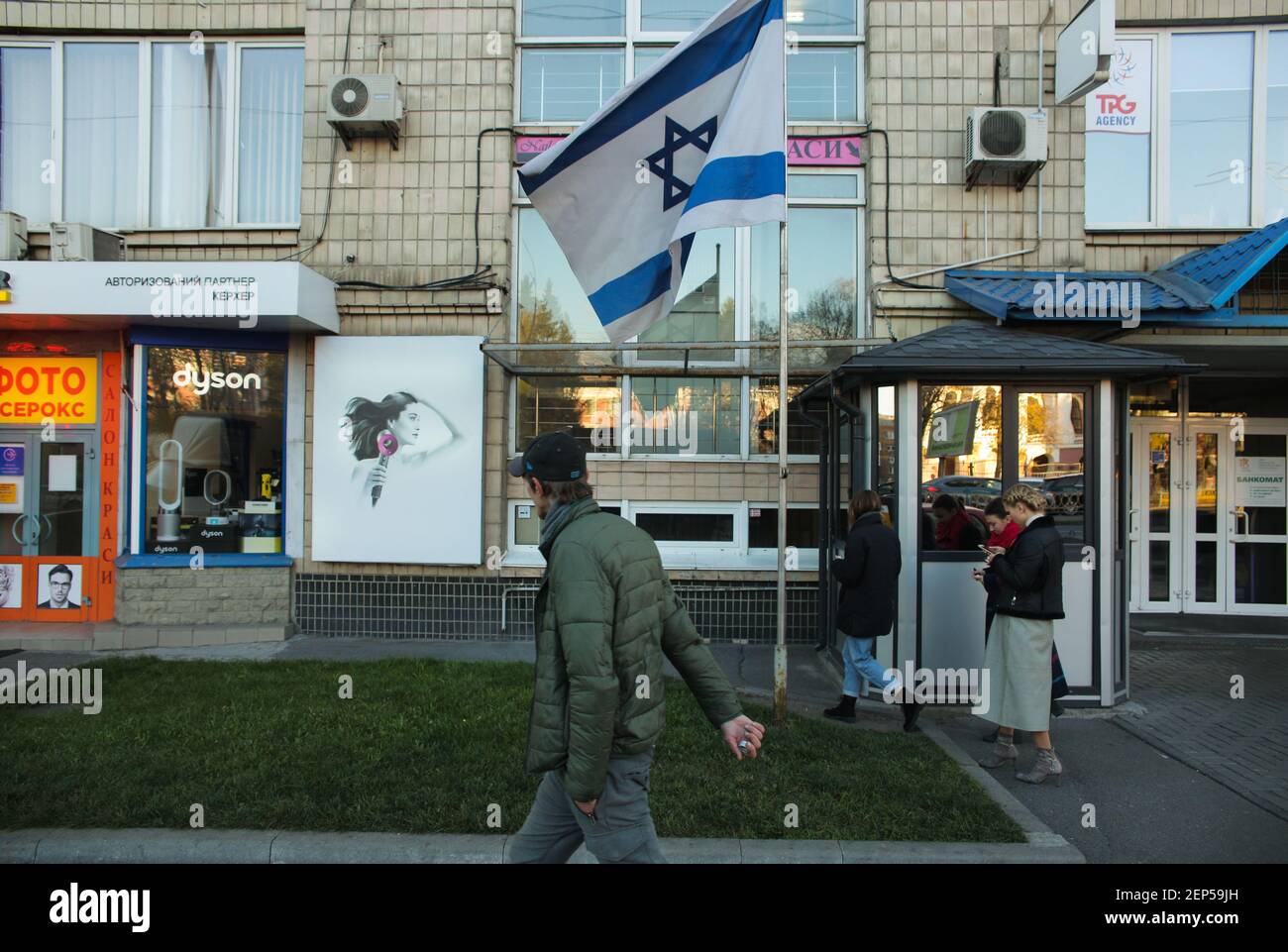 People walk past the Israeli state flag set in front of the building ...