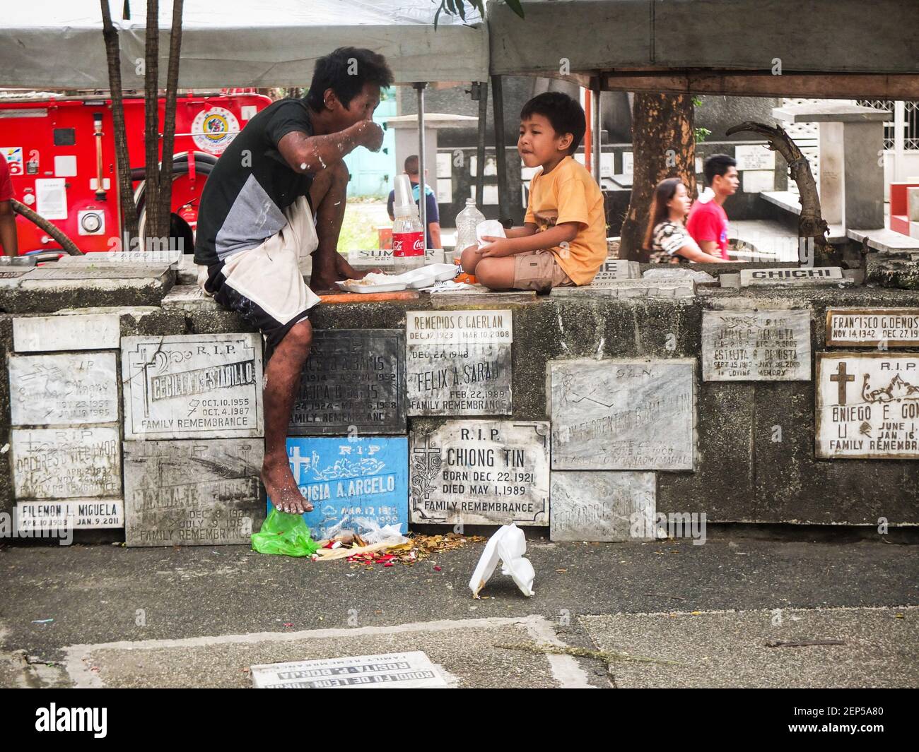 A father and his son eat food at the tombs. Filipinos prepares for the ...