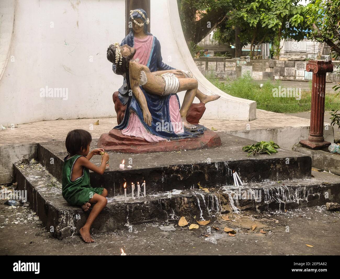 A young boy picks drops of candle wax at the tomb. Filipinos prepares ...