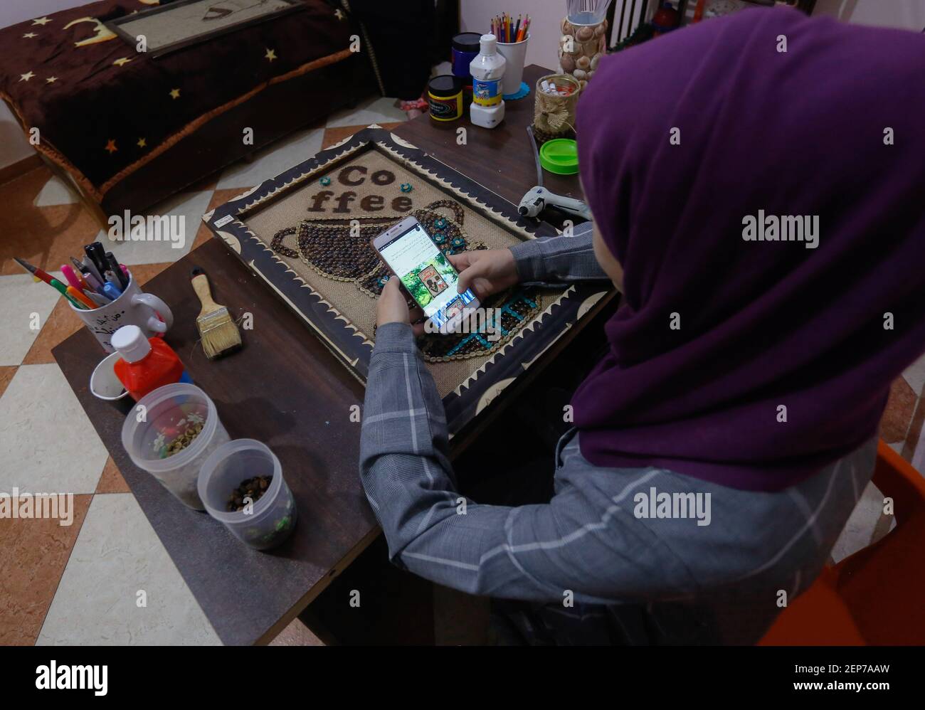 Hala Abu Kaoud holds a mobile phone and displays her paintings online ...