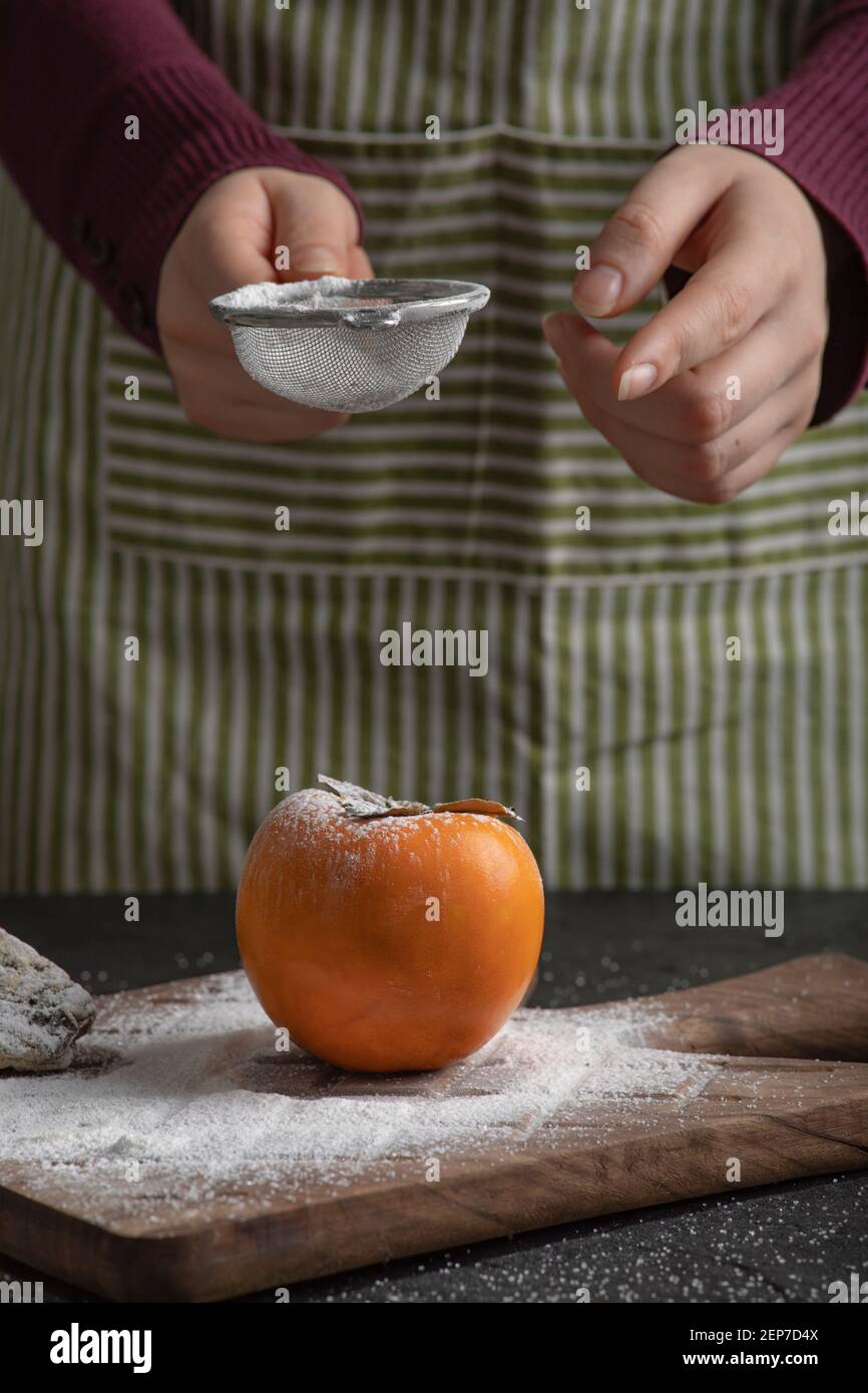 Female cook spilling flour to sweet persimmon in kitchen Stock Photo ...