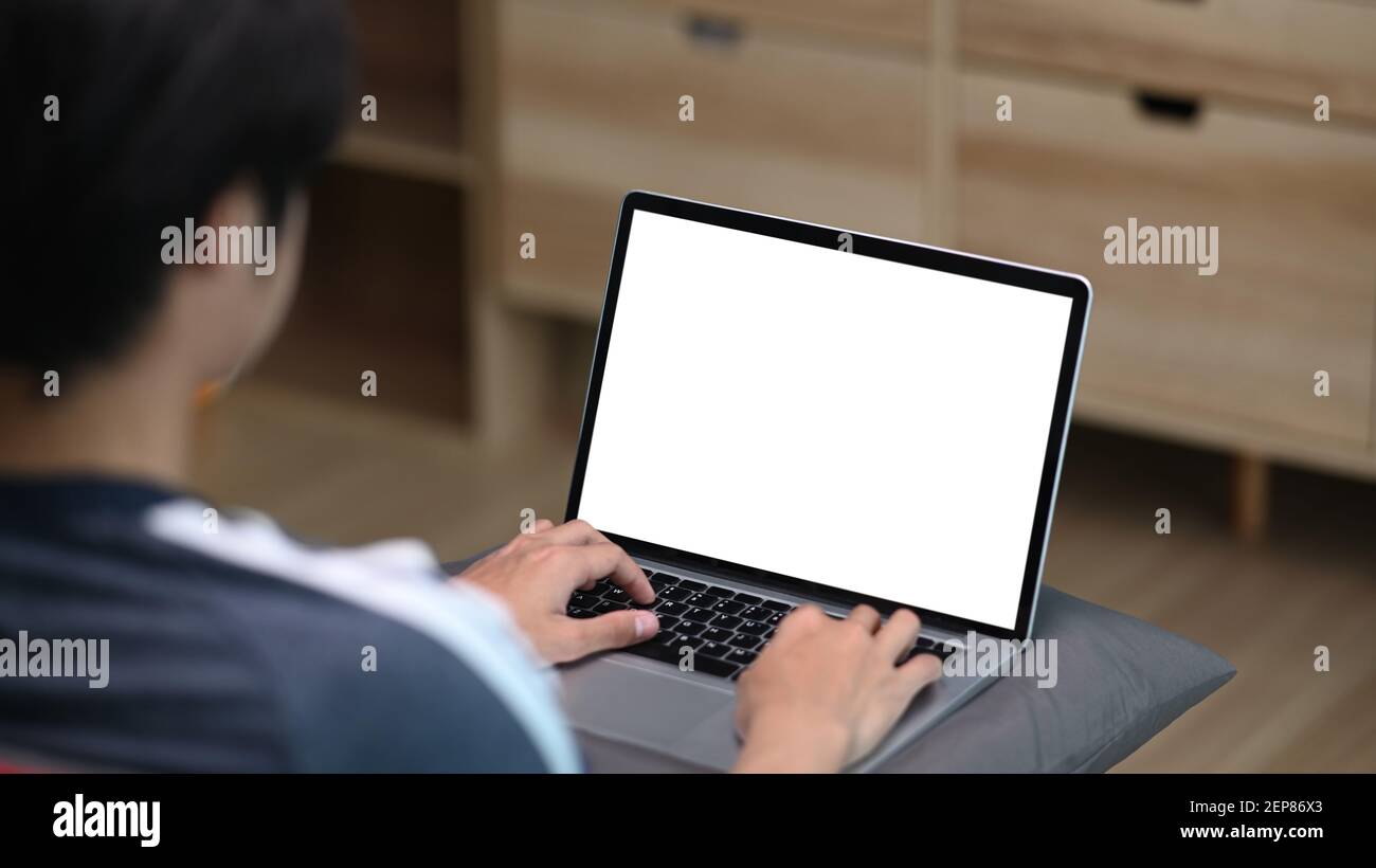 Rear view of casual young man using computer laptop while sitting on couch in living room Stock ...