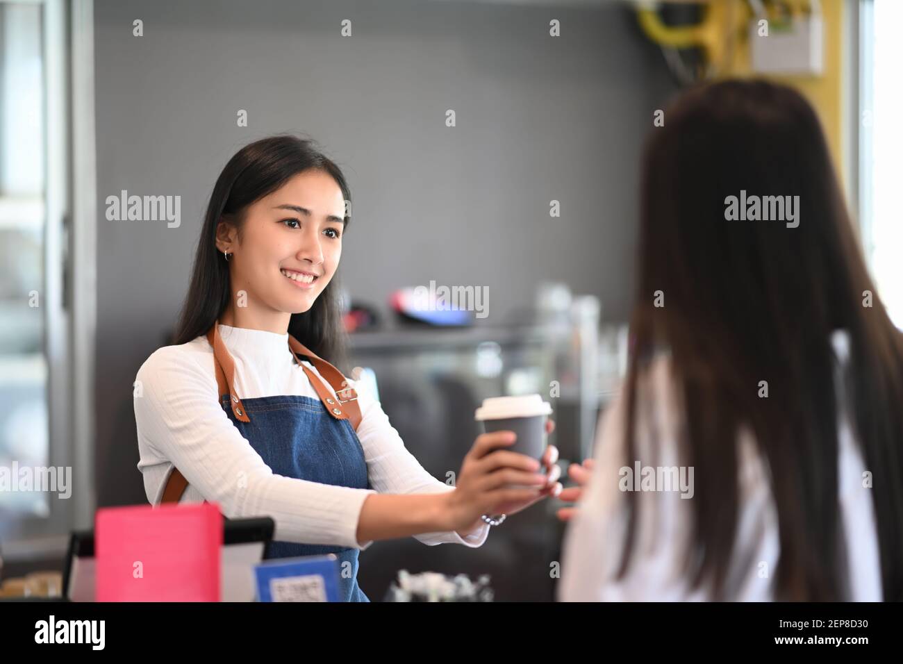 Young female waitress giving takeaway coffee cup to customers in coffee ...