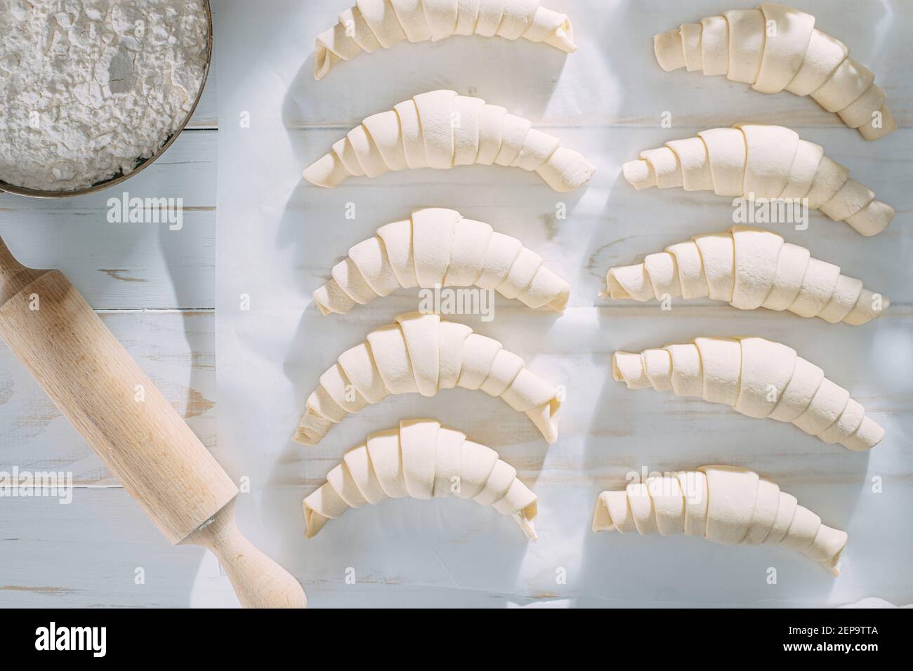 rolled croissant dough and ready for baking on a white wooden table on ...