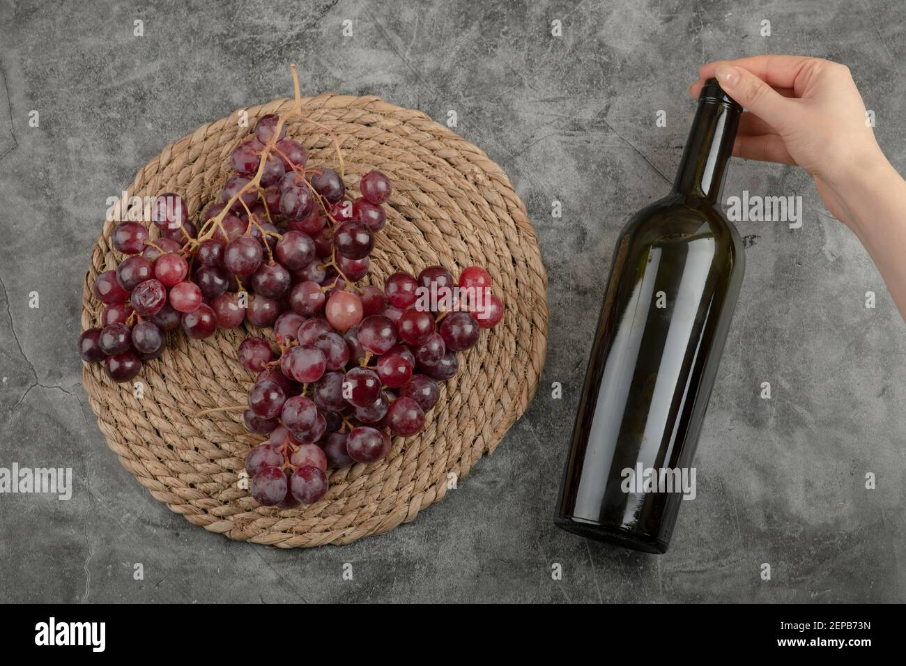 Cluster of red grapes and woman hand holding bottle of wine on marble surface Stock Photo - Alamy