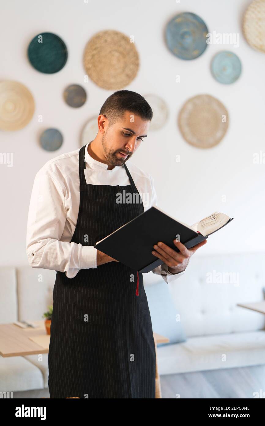 Young chef checking reservations in restaurant wearing uniform and kitchen gown Stock Photo Alamy