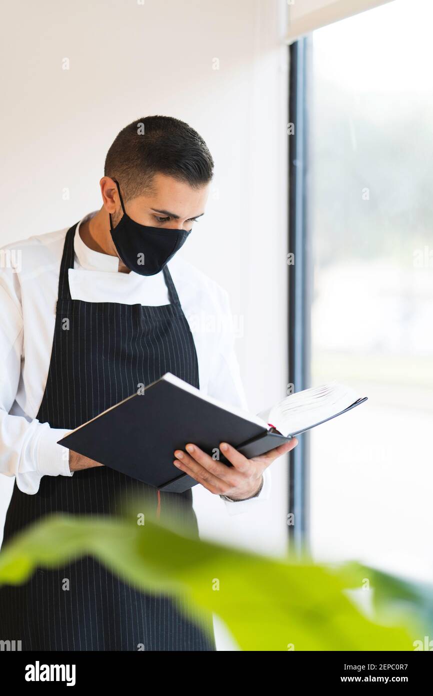 Young chef checking reservations talking by phone in restaurant wearing ...