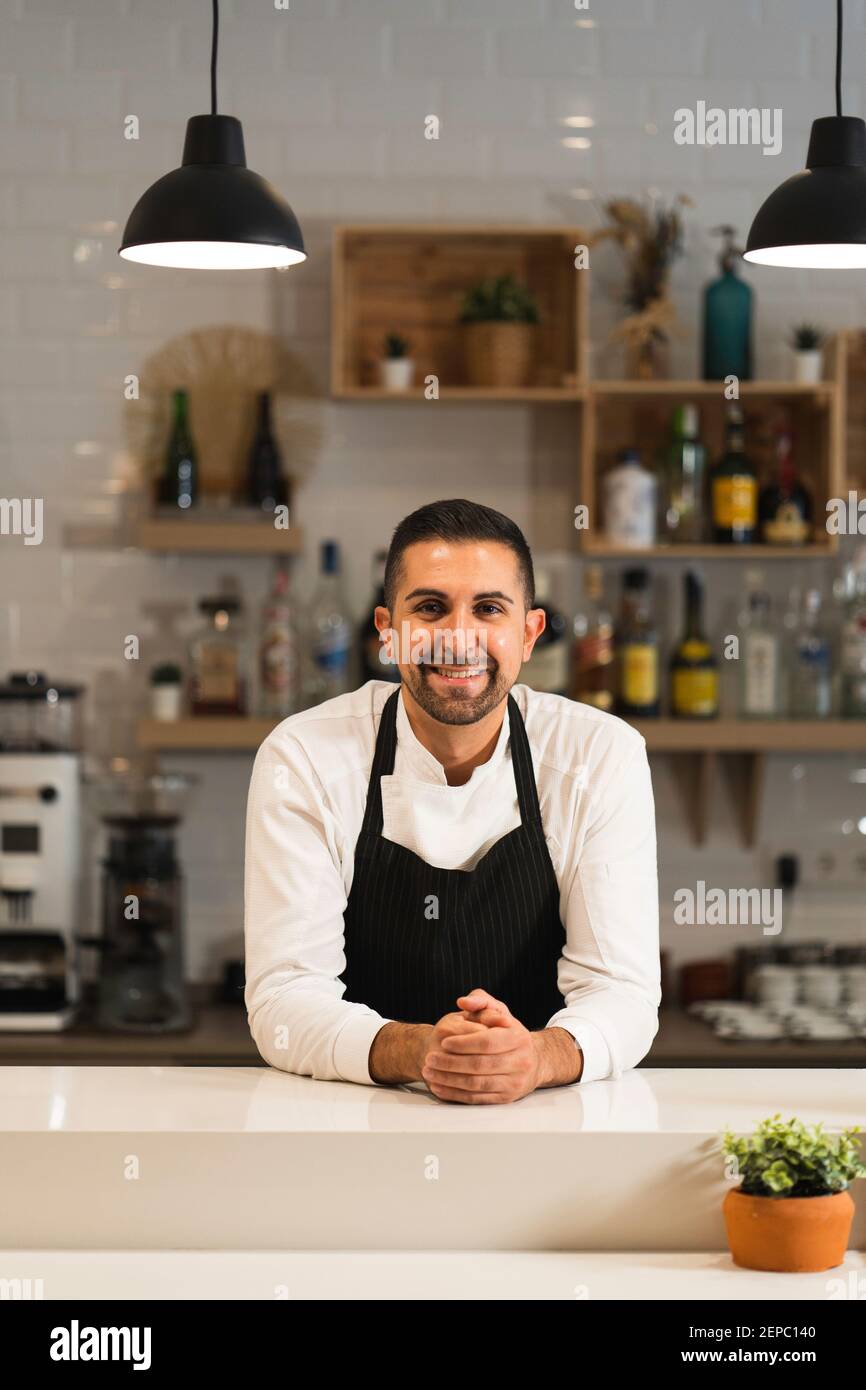 Portrait of a Happy young chef posing wearing uniform and kitchen gown ...