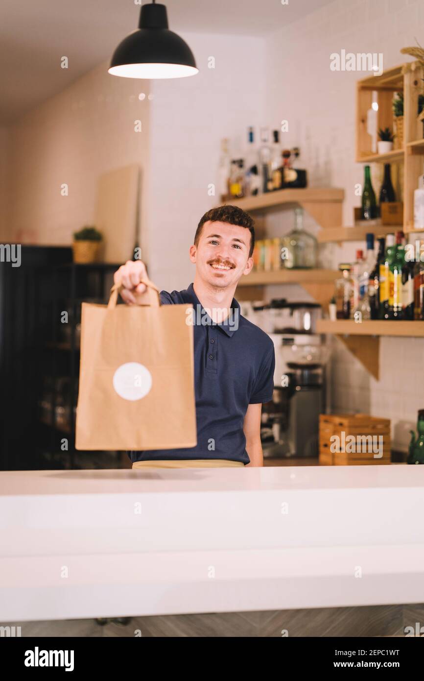 portrait of a smiling professional waiter handing over a recycled paper ...
