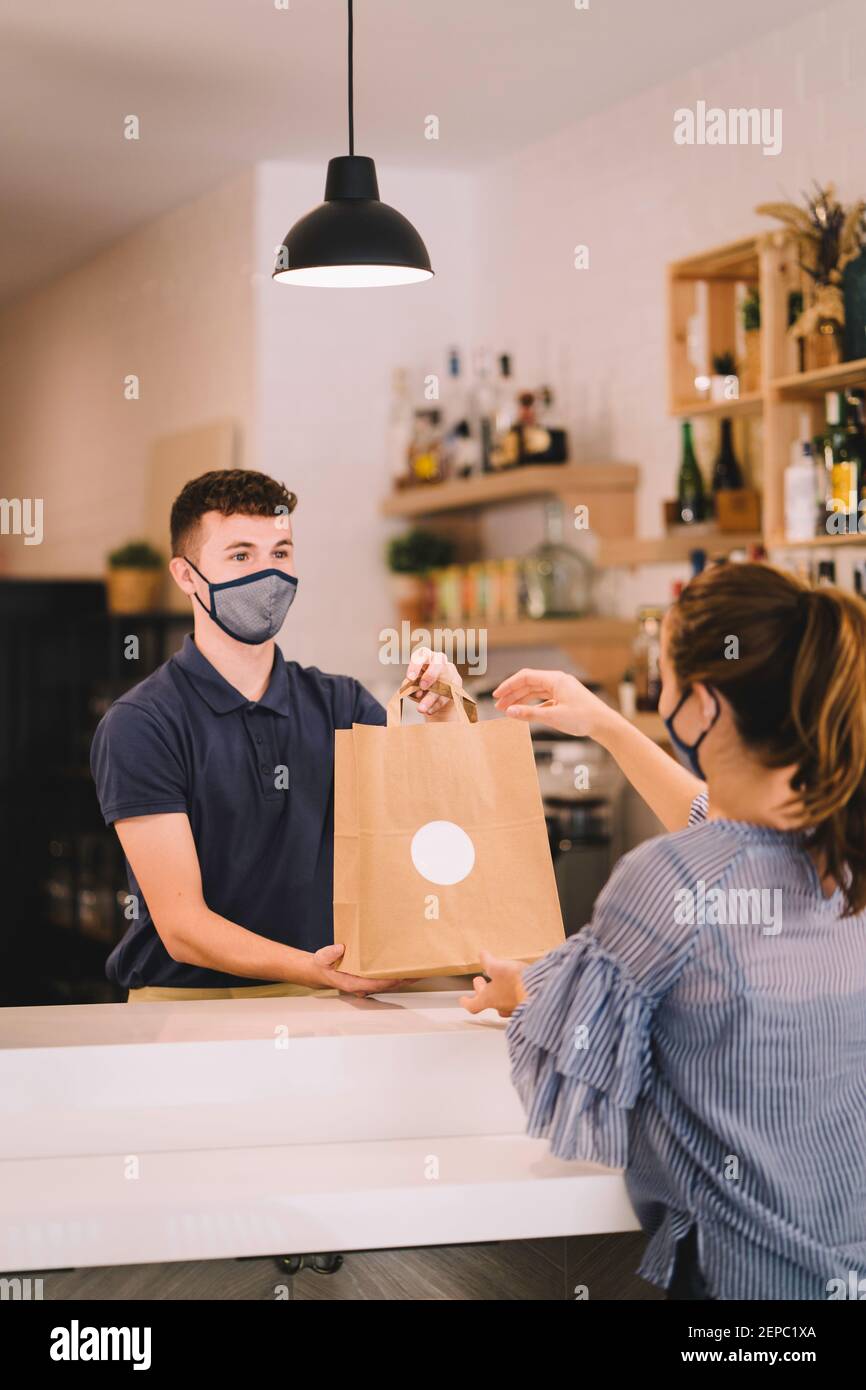 Portrait of a professional waiter handing to a customer a takeaway ...