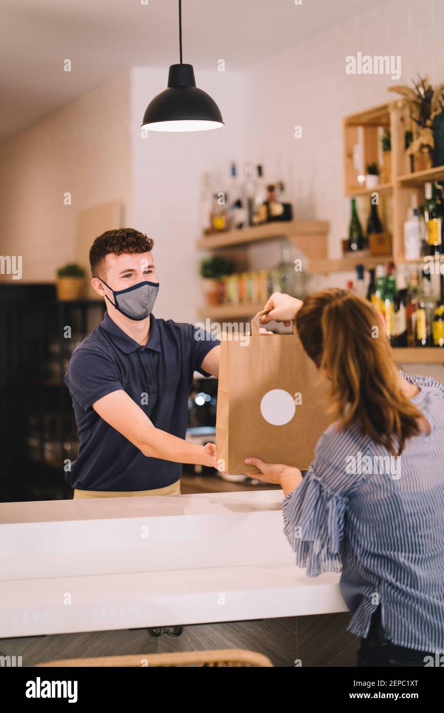 Portrait of a professional waiter handing to a customer a takeaway ...