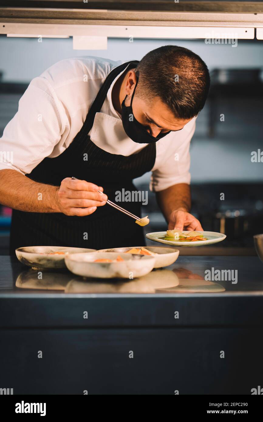 Close-up of a male chef with mask decorating food in ceramic dishes ...