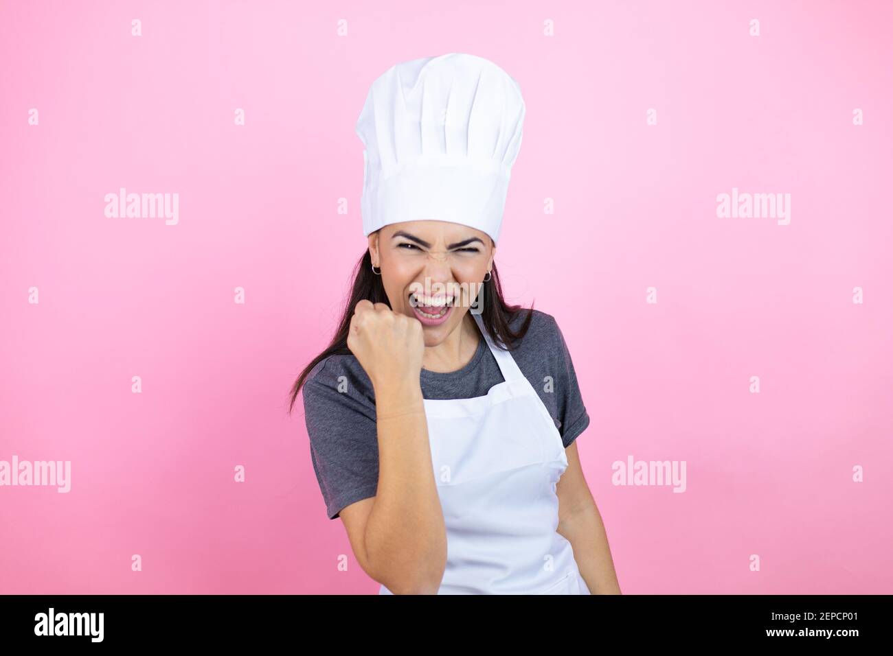Young hispanic woman wearing baker uniform over pink background angry ...