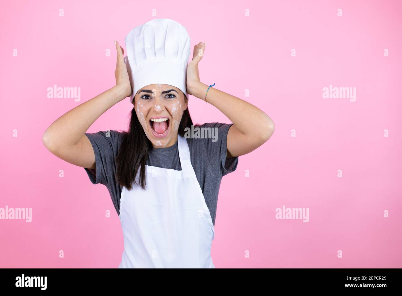 Young hispanic woman wearing baker uniform with flour on the face over ...