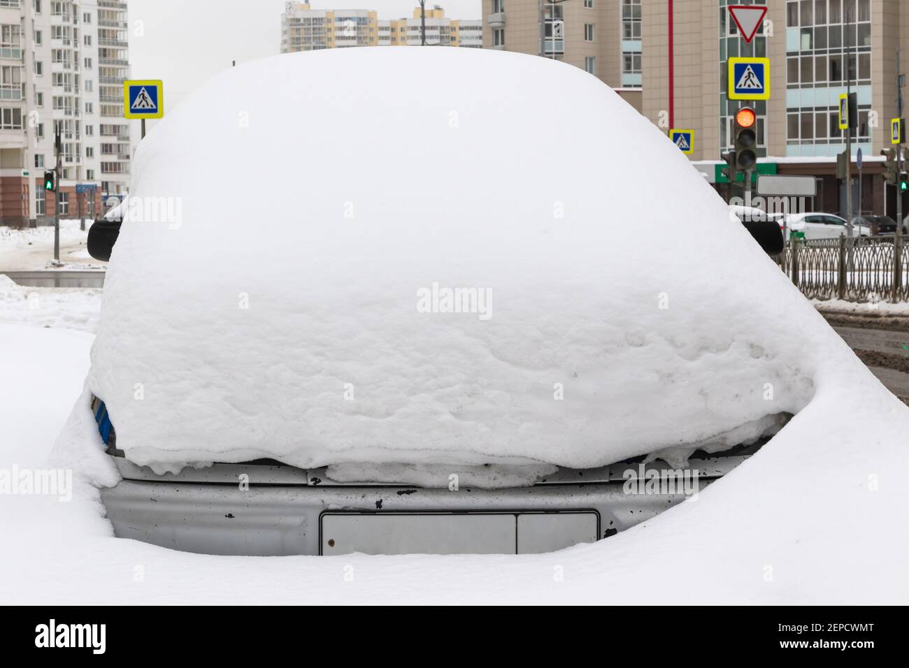 old abandoned broken car parked by the road under a large layer of snow ...