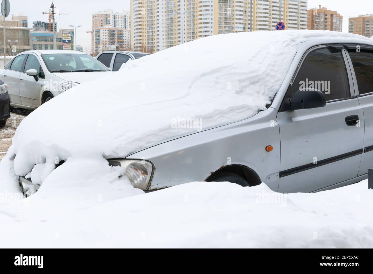 old abandoned broken car parked by the road under a large layer of snow ...