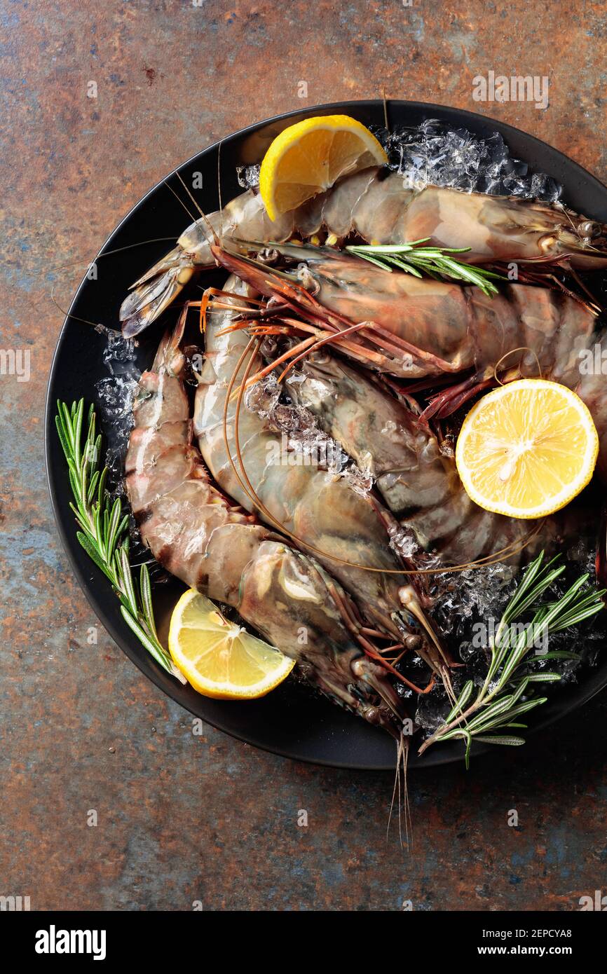 Fresh tiger prawns in a black plate with lemon, rosemary, and crushed ...