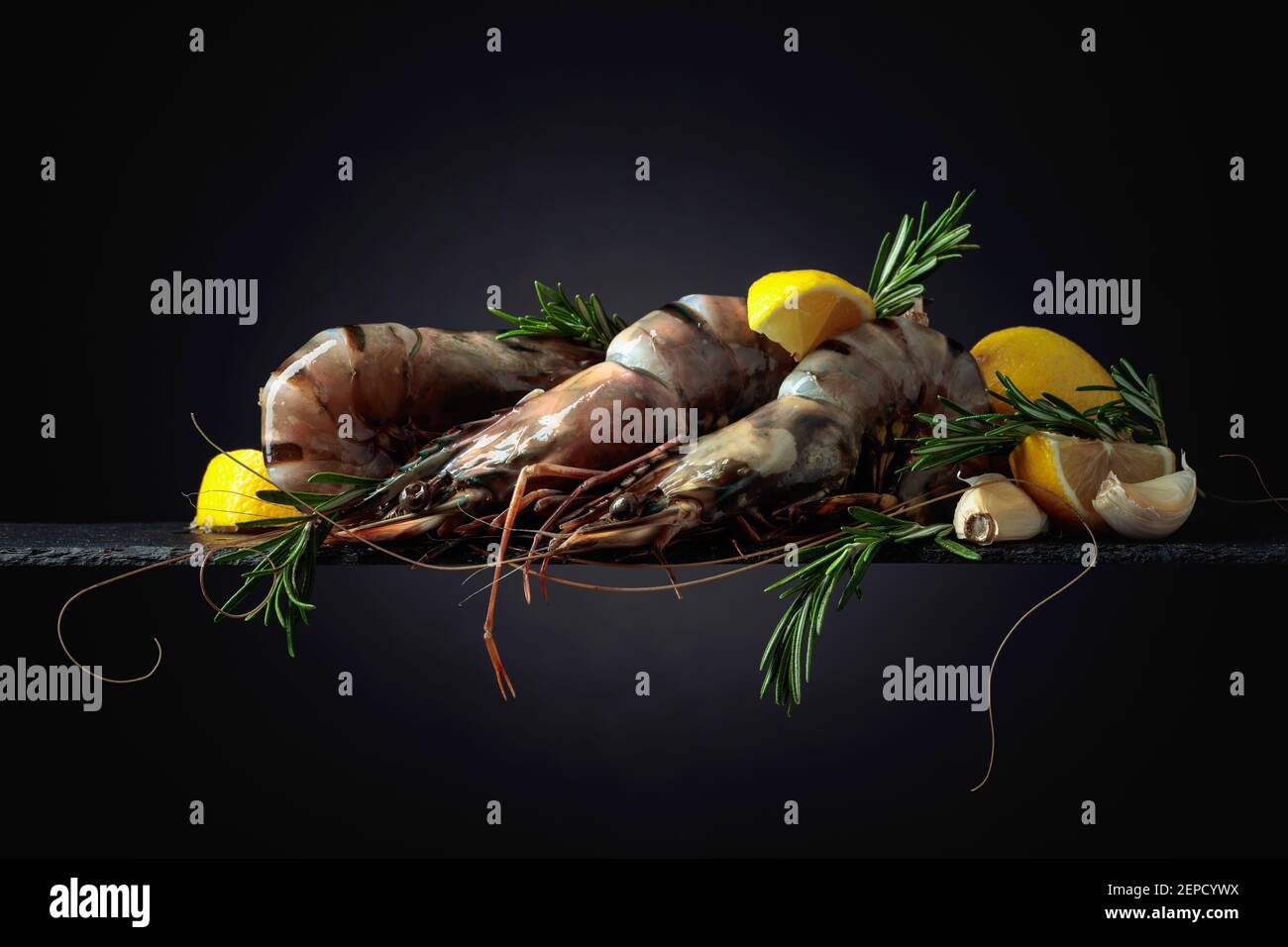 Fresh tiger prawns with lemon, rosemary, and garlic on a black ...