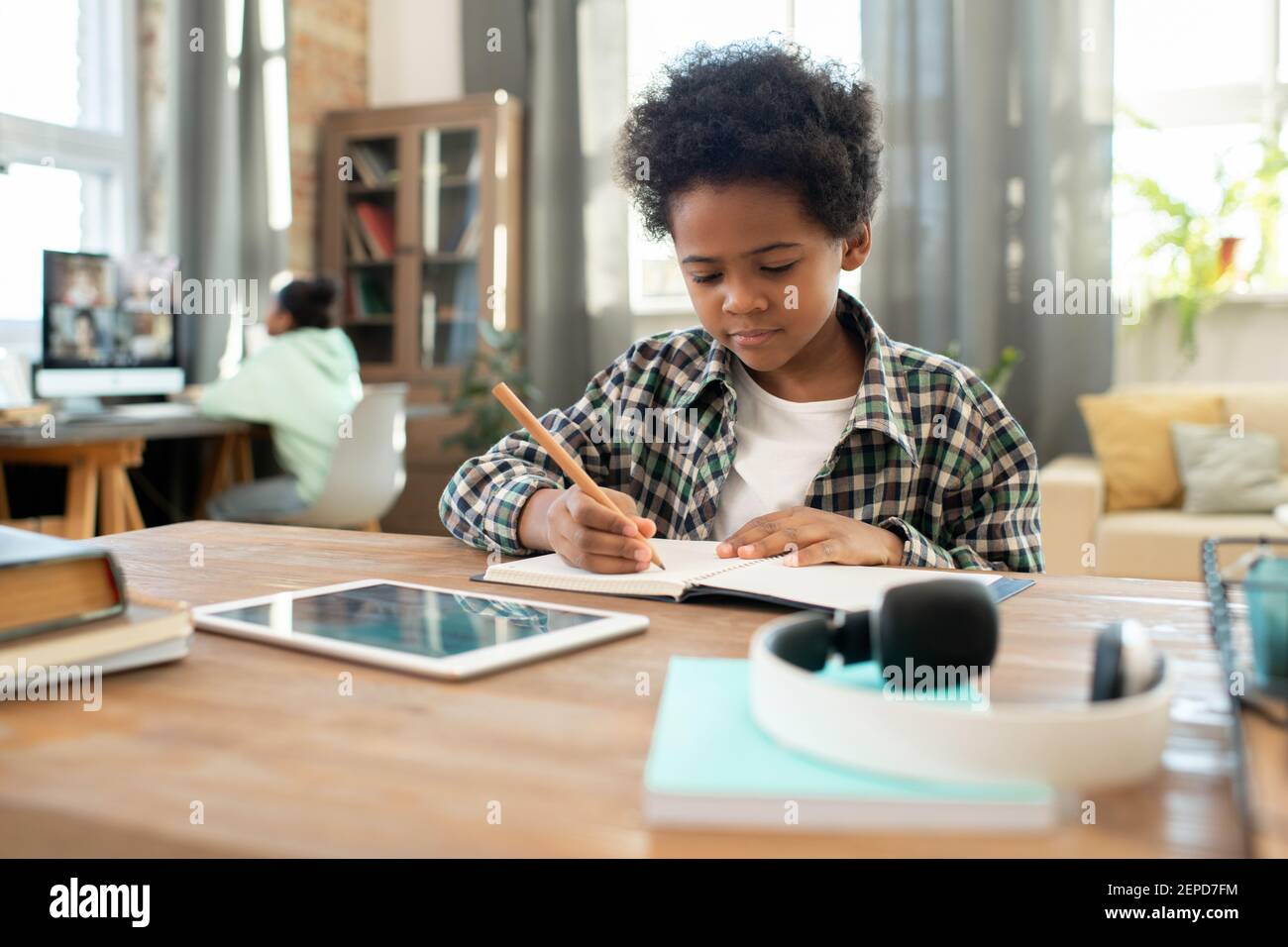 Cute elementary African schoolboy with pencil making notes in copybook ...