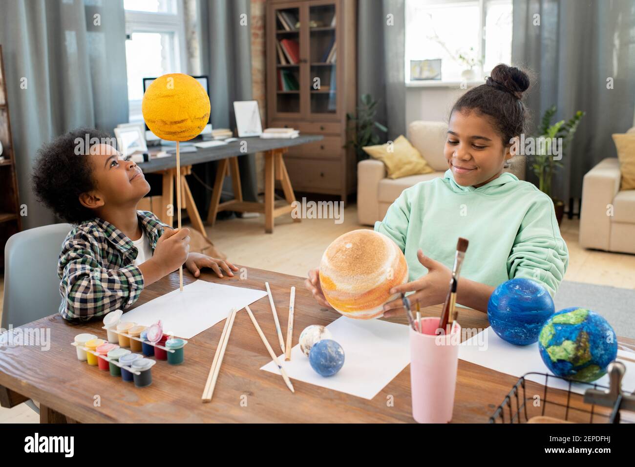 Two adorable mixed-race elementary schoolkids making planets while ...
