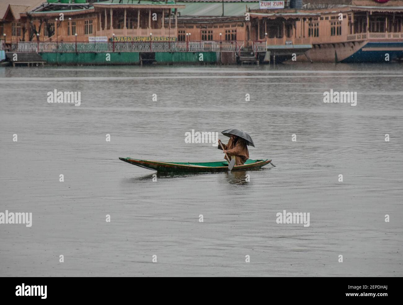 A boatman under an umbrella rows his boat on Dal lake during rainfall ...