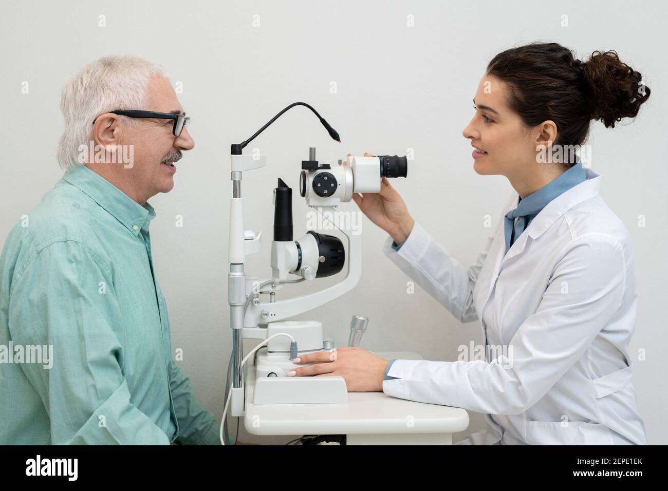 Side view of happy young female ophthalmologist using medical equipment ...