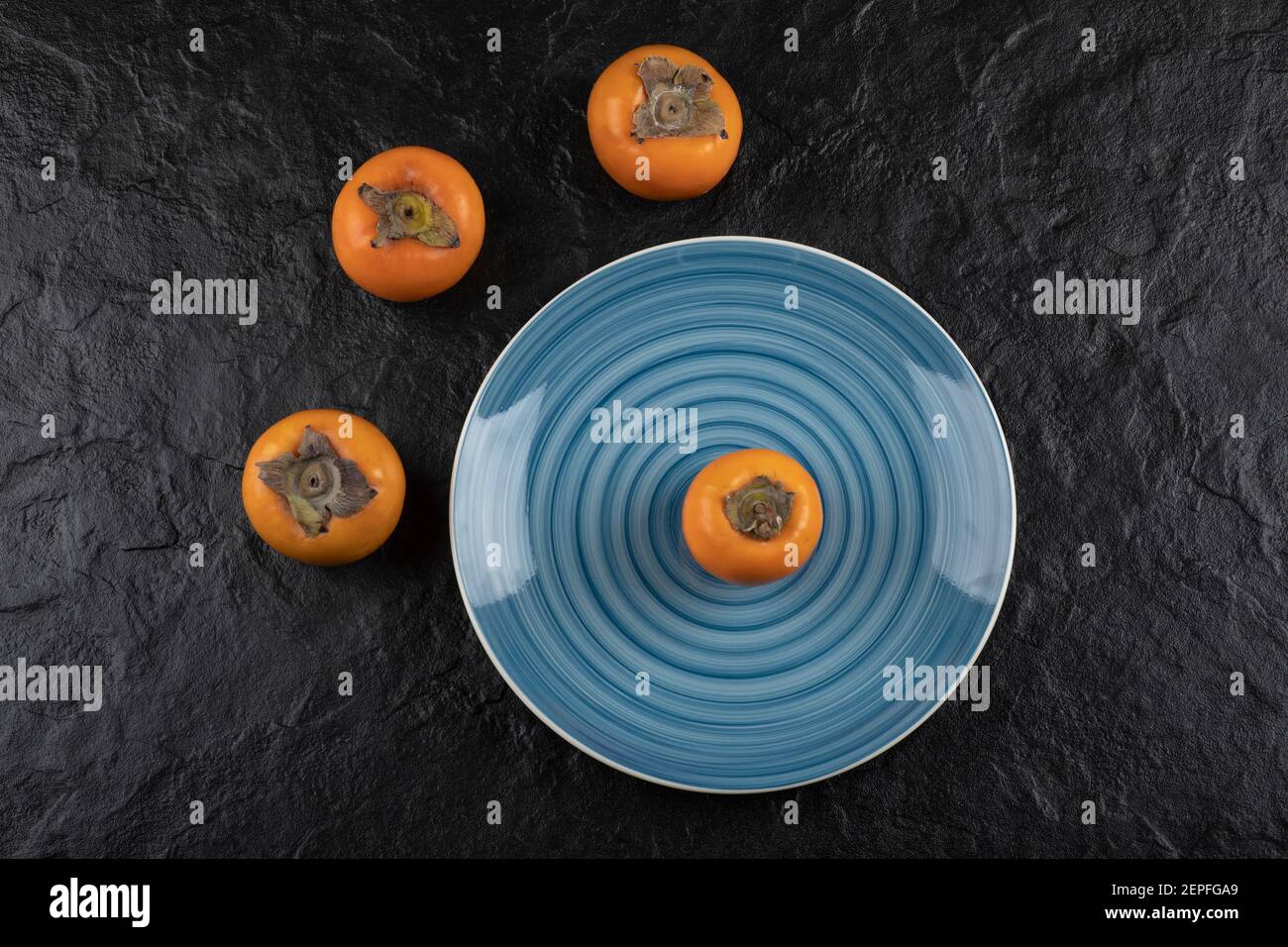 Blue plate of delicious ripe fuyu persimmons on black surface Stock ...
