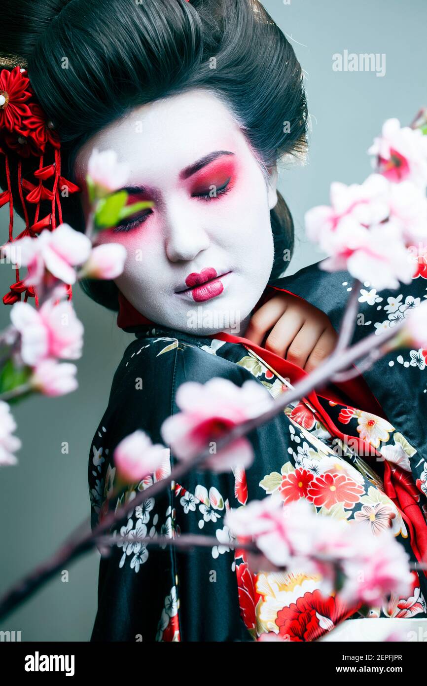 young pretty geisha in black kimono among sakura, asian ethno close up ...