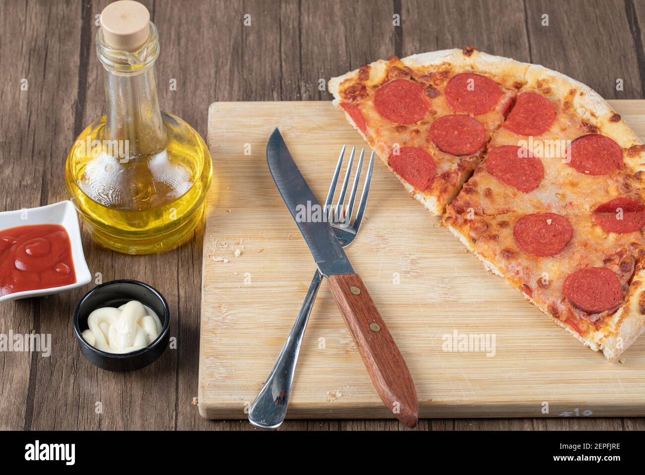 Half of pepperoni pizza on wooden plate with sauces and oil Stock Photo - Alamy