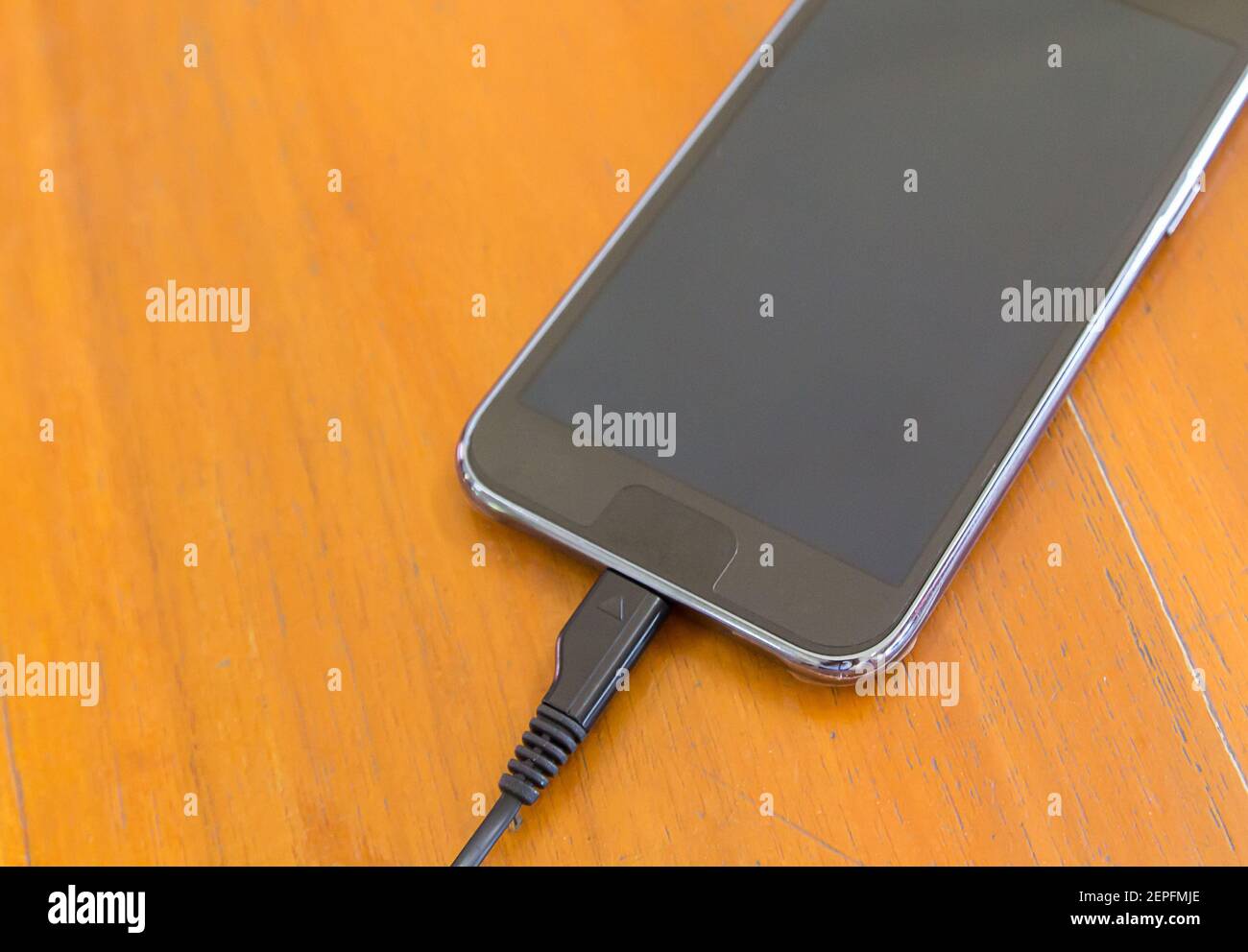 Close up of smart phone charging with USB cable on wooden texture ...