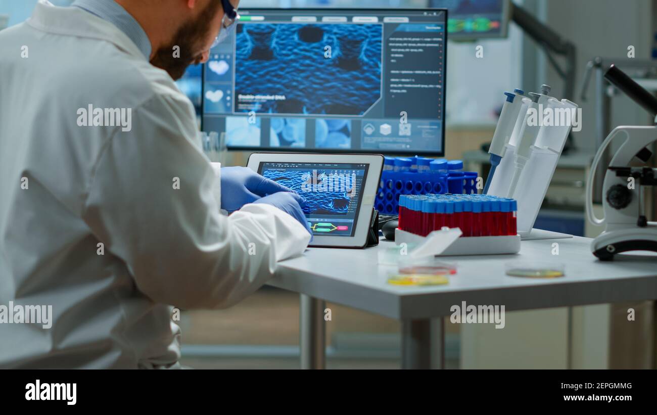 Biochemist checking manifestations of virus looking in tablet with ...