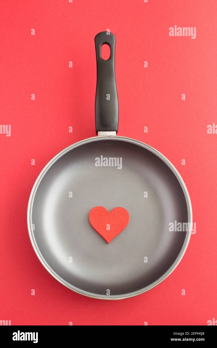 Top view of red heart in a frying pan on the red surface. Location ...