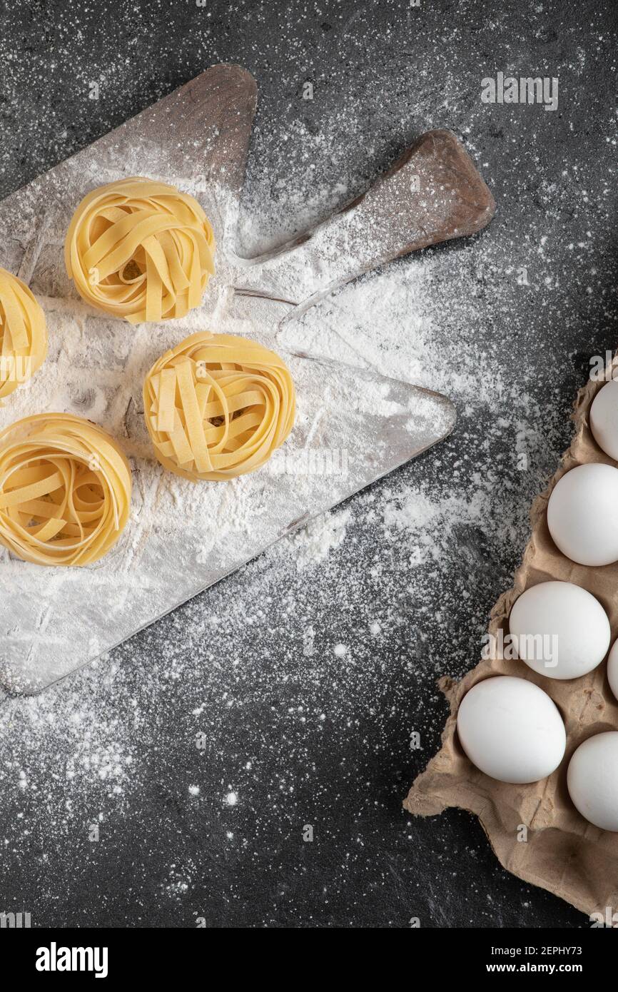 Raw fresh tagliatelle nests with flour on wooden board and eggs Stock ...