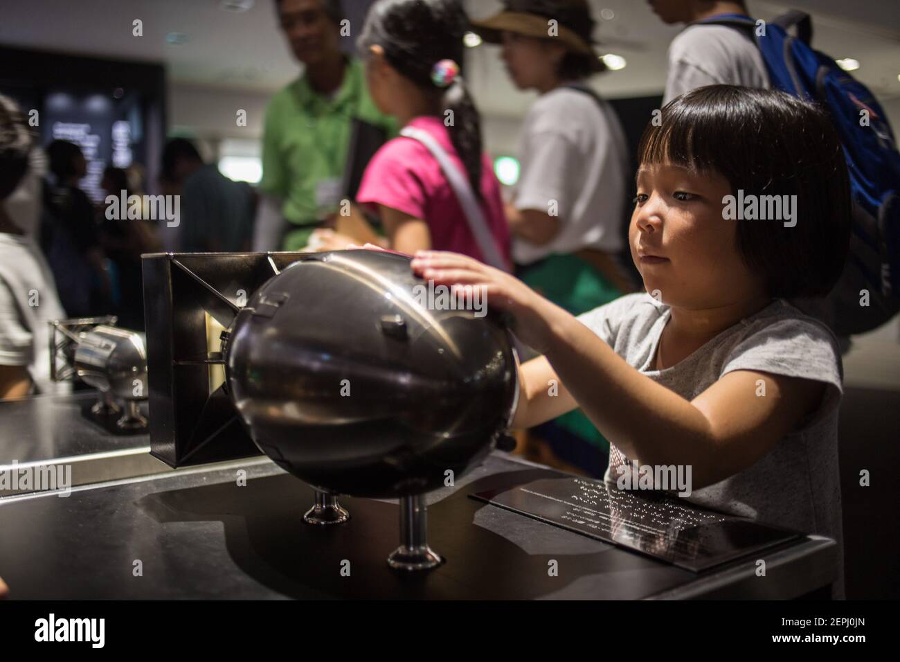 A little girl is touching a miniature scale model of the atomib bomb ...