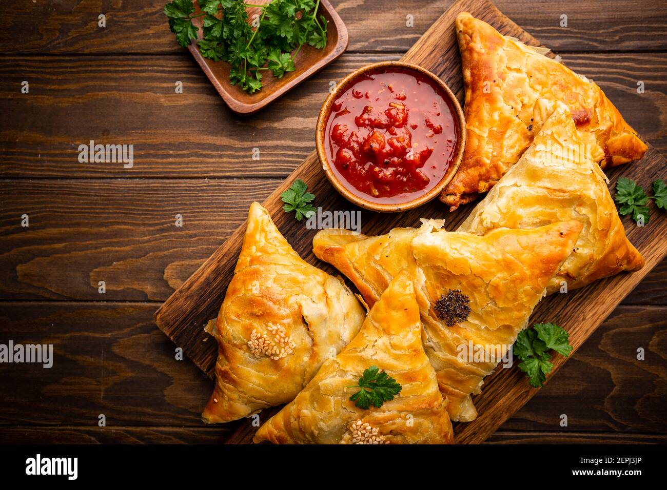 Samsa or samosas with meat and vegetables with tomato sauce on wooden background. Traditional ...