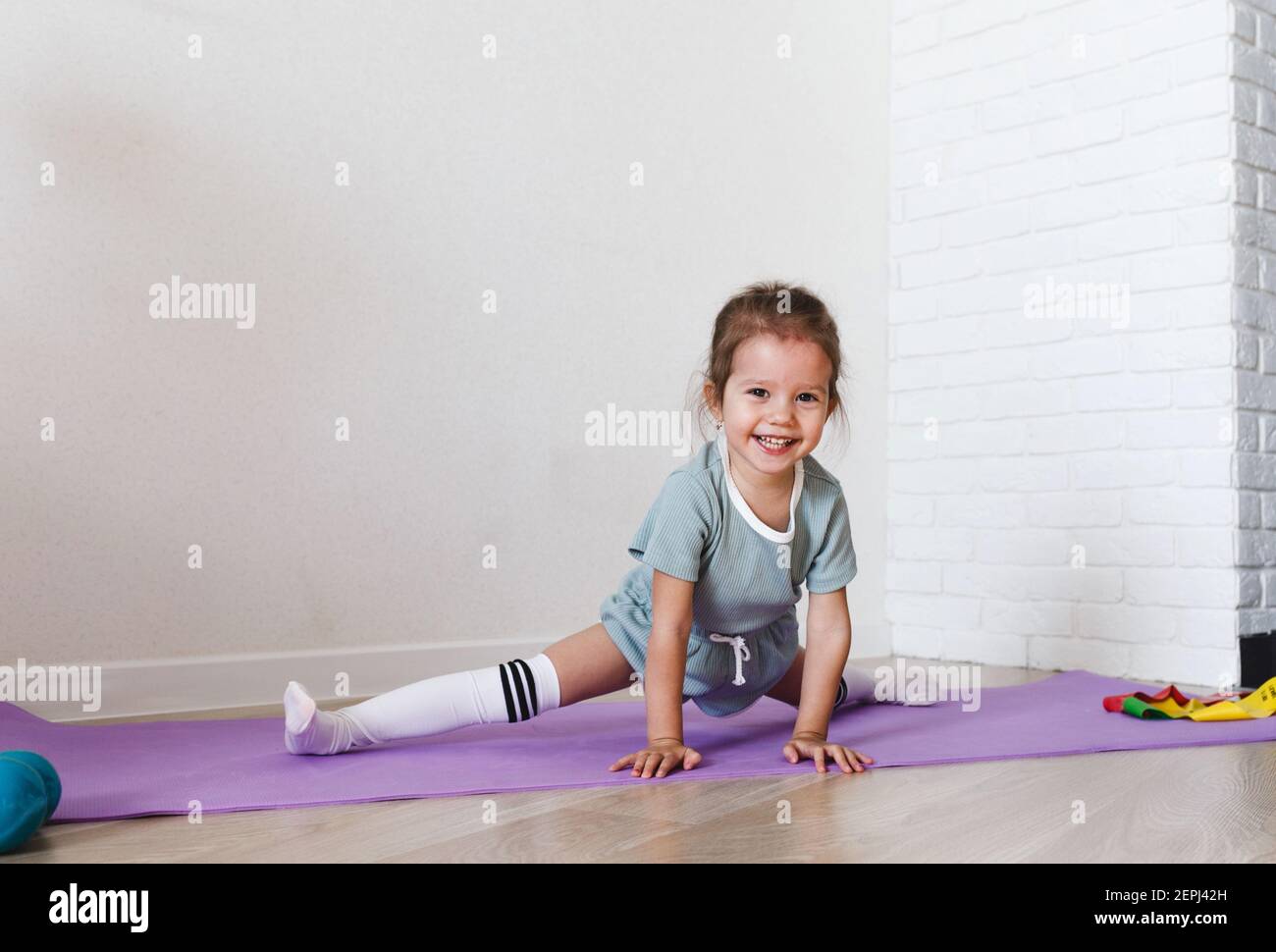 A little girl sits on the splits during a fitness class at home. Sports ...