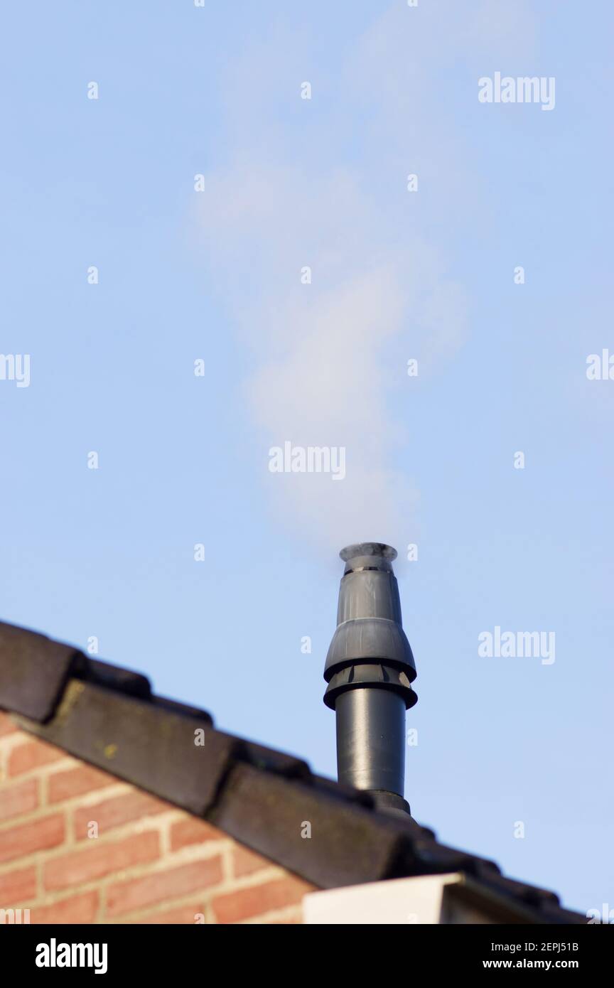 Closeup of a chimney system of a house with smoke and a clear blue sky ...