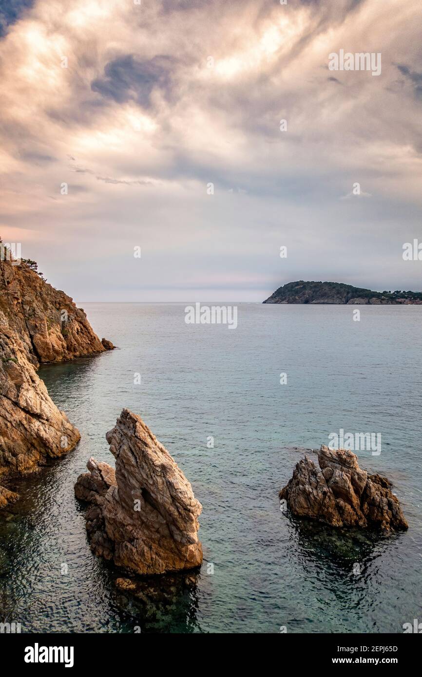 Costa Brava cliffs at sunset with rocks in the foreground and a sky ...