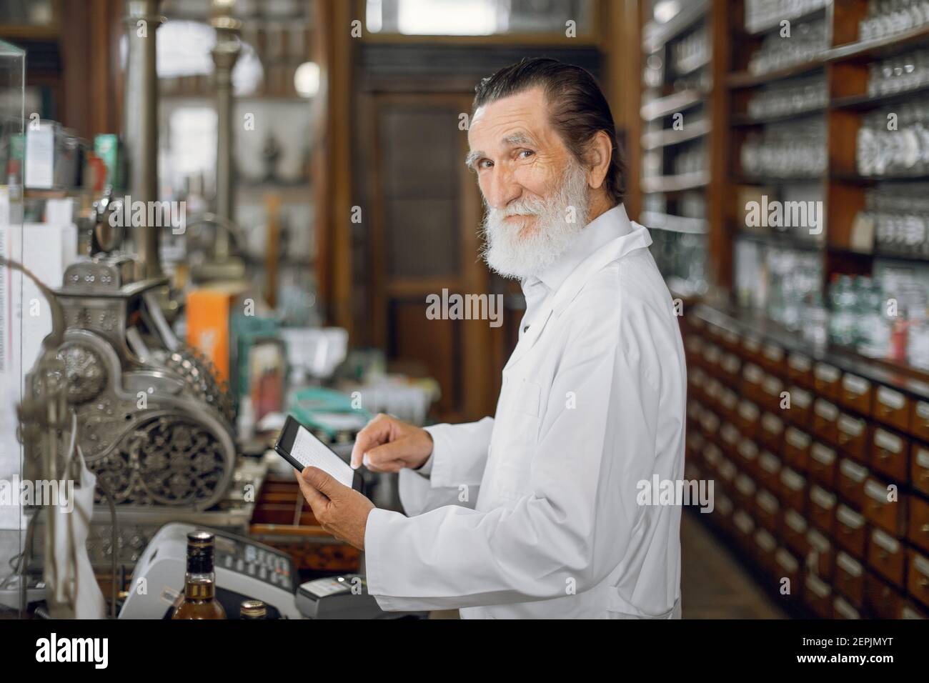 Pleasant senior male pharmacist working on digital tablet. Shelf with ...