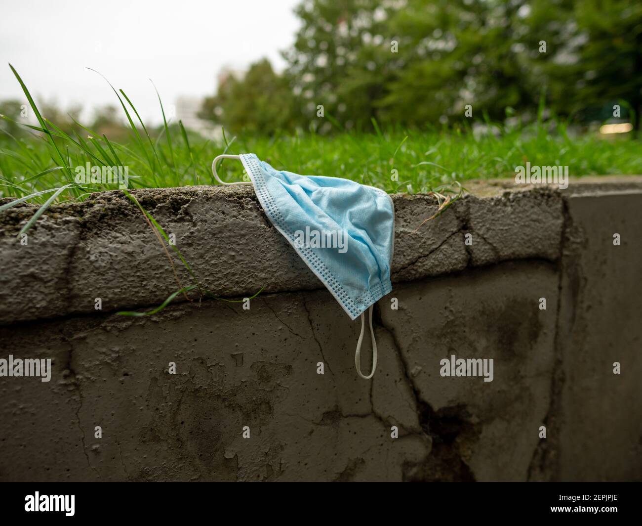 Used face mask on a wall next to green grass as environmental pollution ...