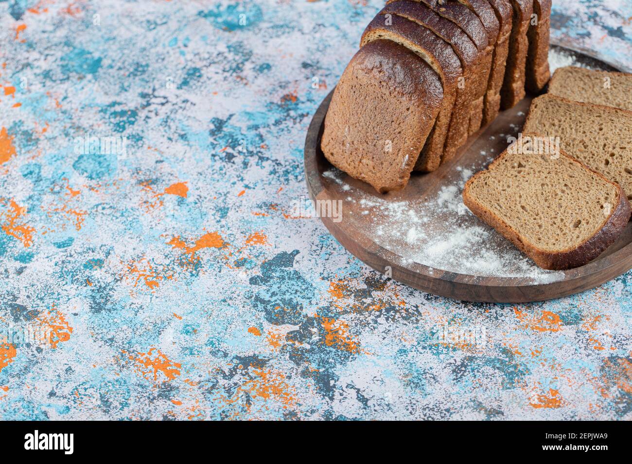 Slices of brown bread with flour on a wooden round board Stock Photo ...