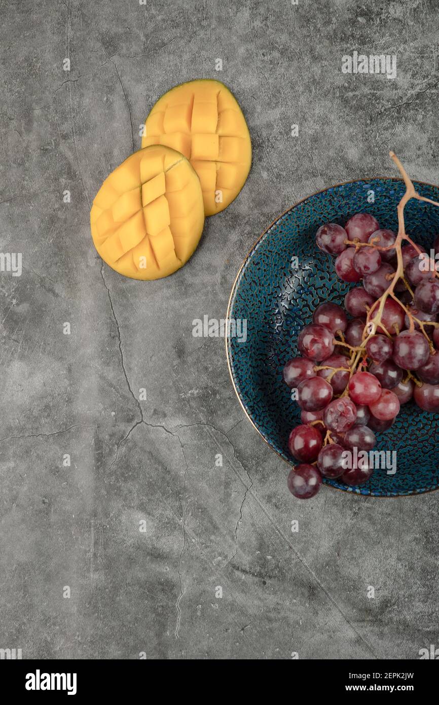 Deep plate of red ripe grapes and sliced mango on marble surface Stock ...
