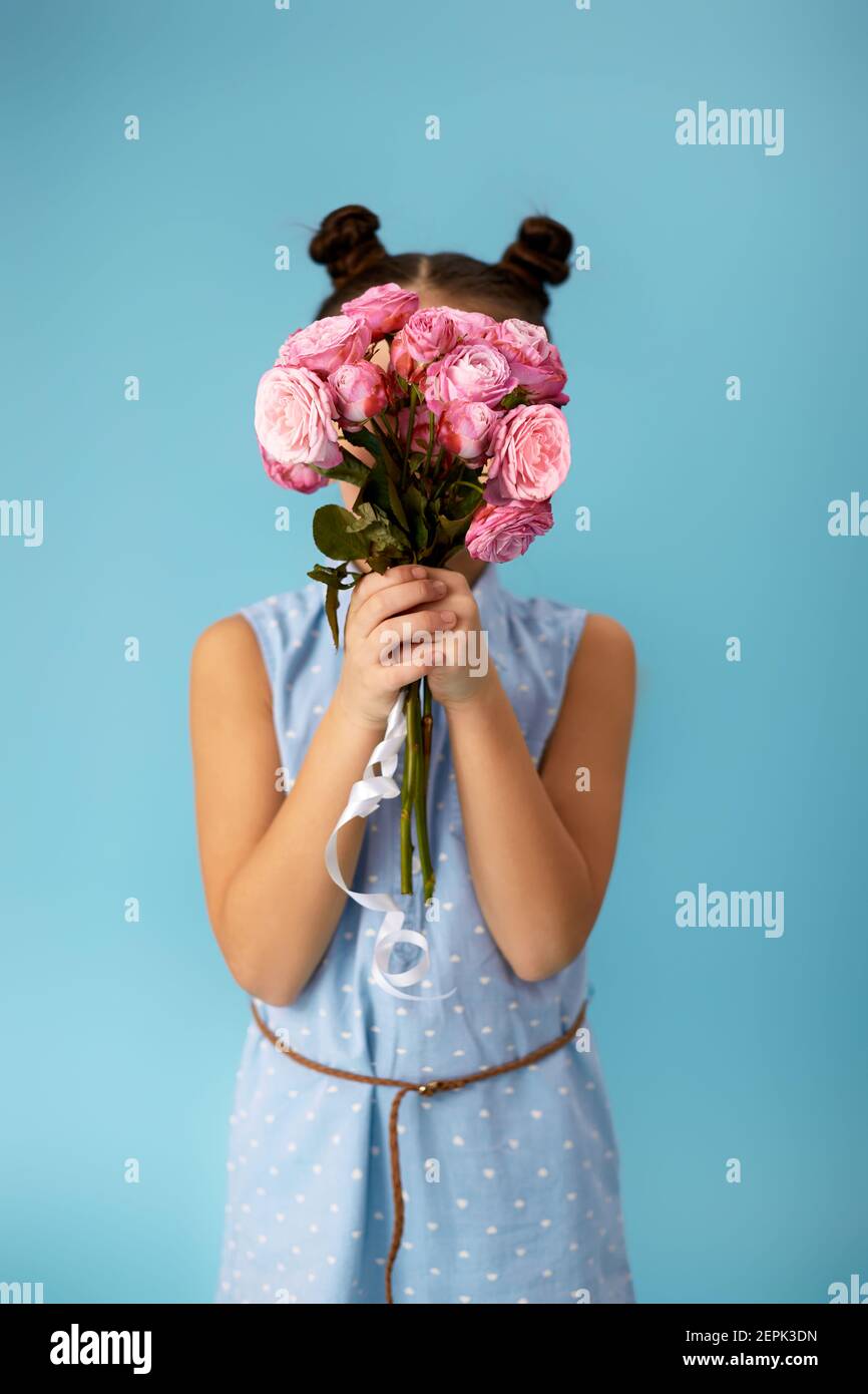 little child girl holding bouquet of roses in front of her face on blue ...