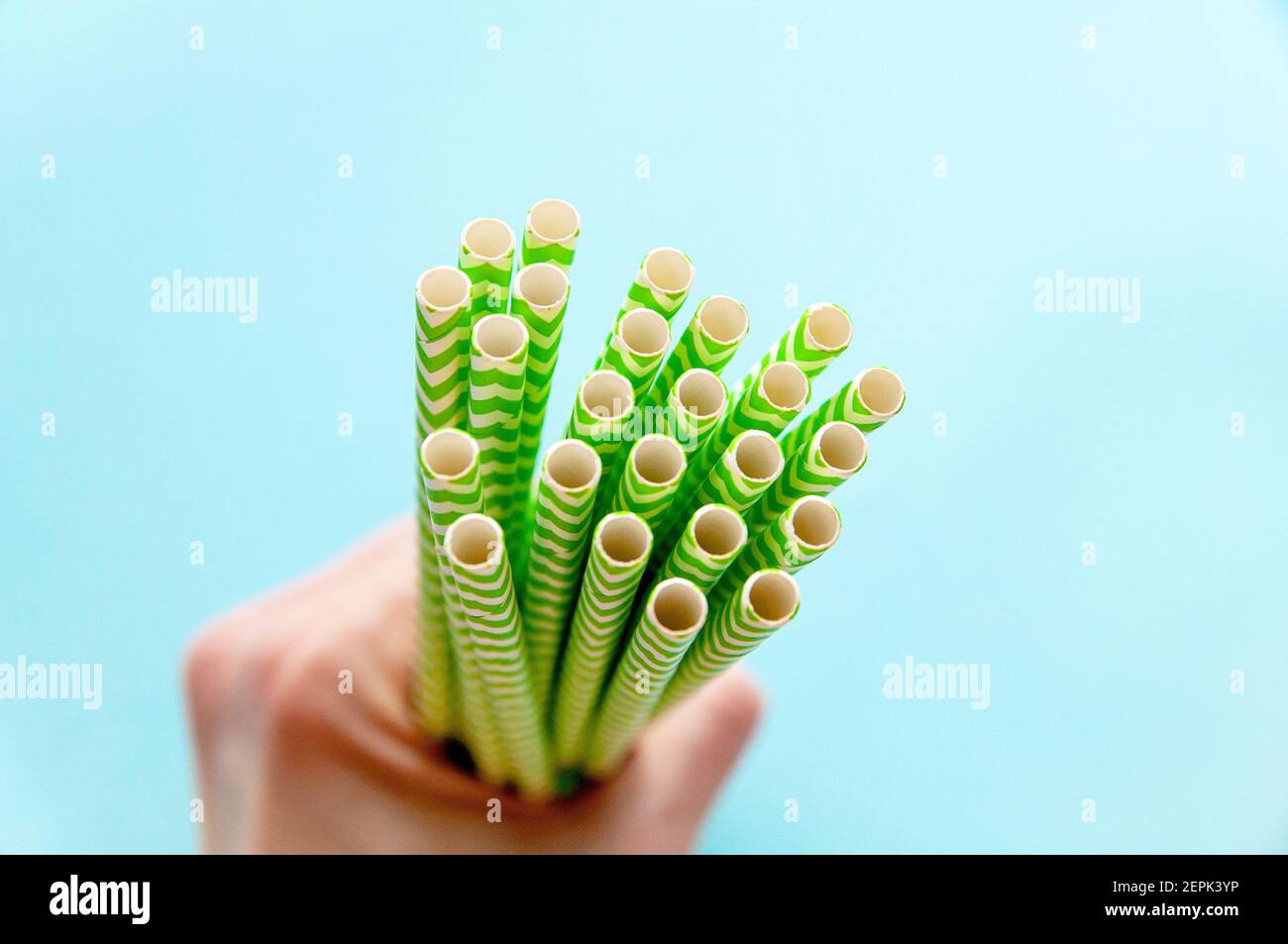 disposable green-white straws are located in the hands against a blue ...