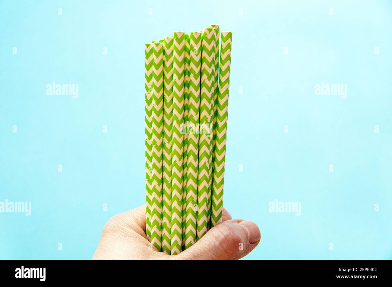 disposable green-white straws are located in the hands against a blue ...