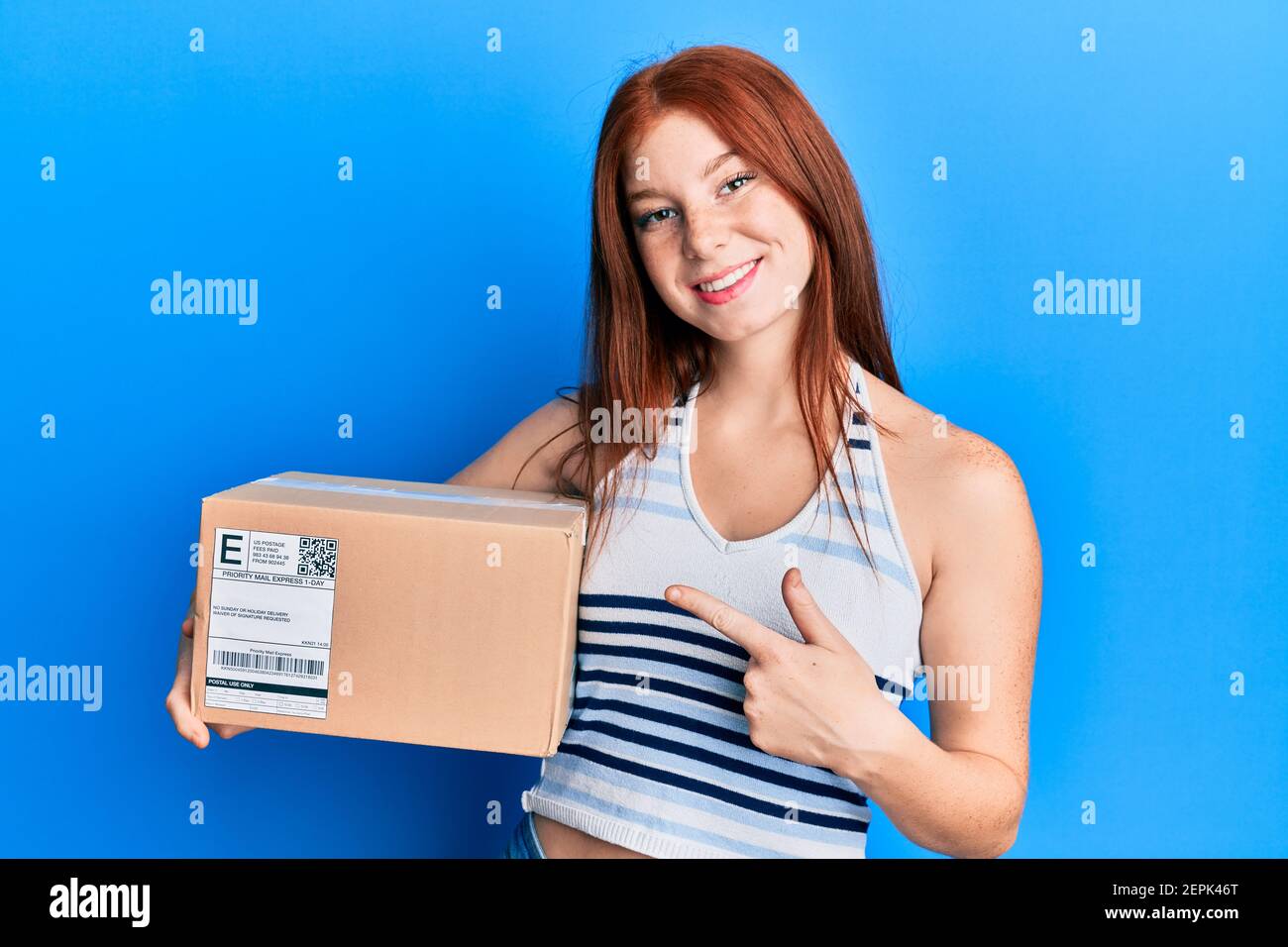 Young red head girl holding delivery package smiling happy pointing ...